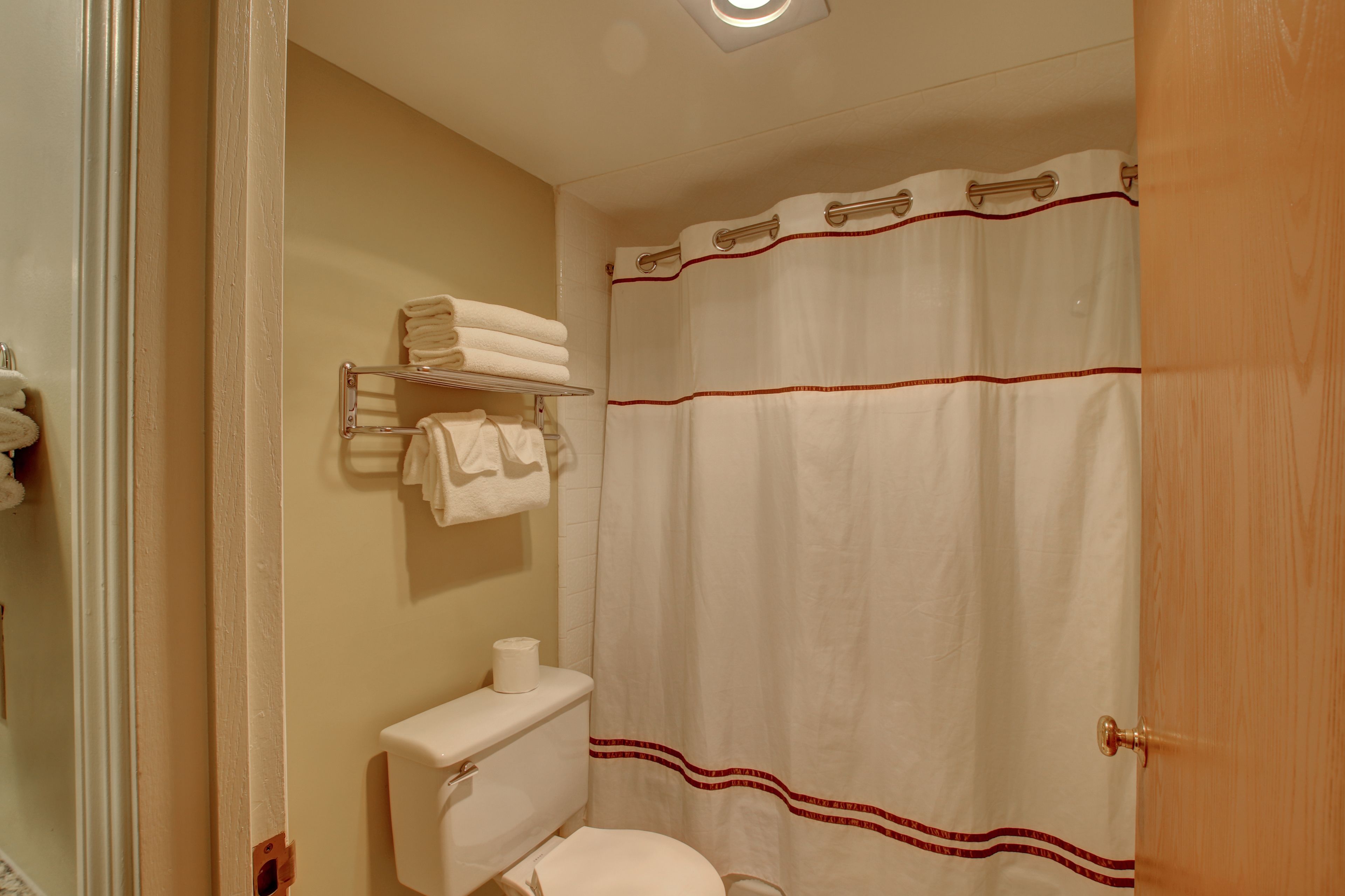 Casa de banho com sanita, um porta-toalhas com toalhas dobradas e cortina de chuveiro com borda decorativa.