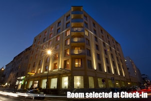 Um hotel de vários andares com área de check-in, janelas iluminadas e um sinal de estacionamento visível.