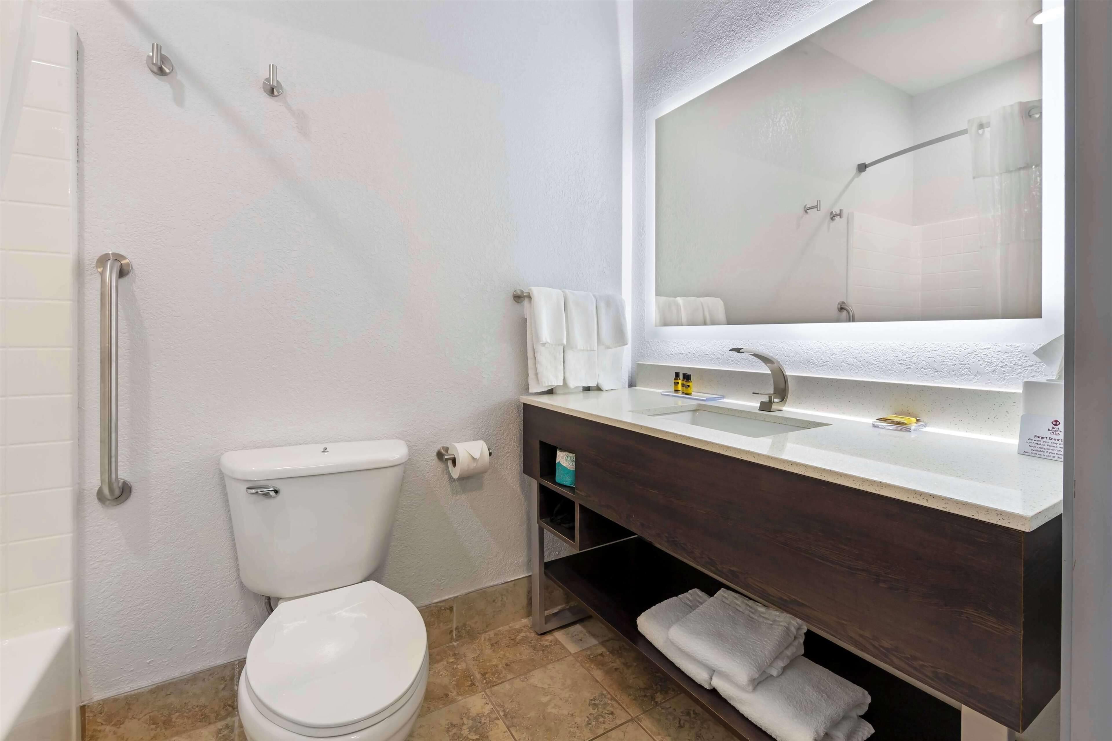 Um banheiro moderno com vaso sanitário branco, pia com bancada escura e um espelho grande acima da pia.