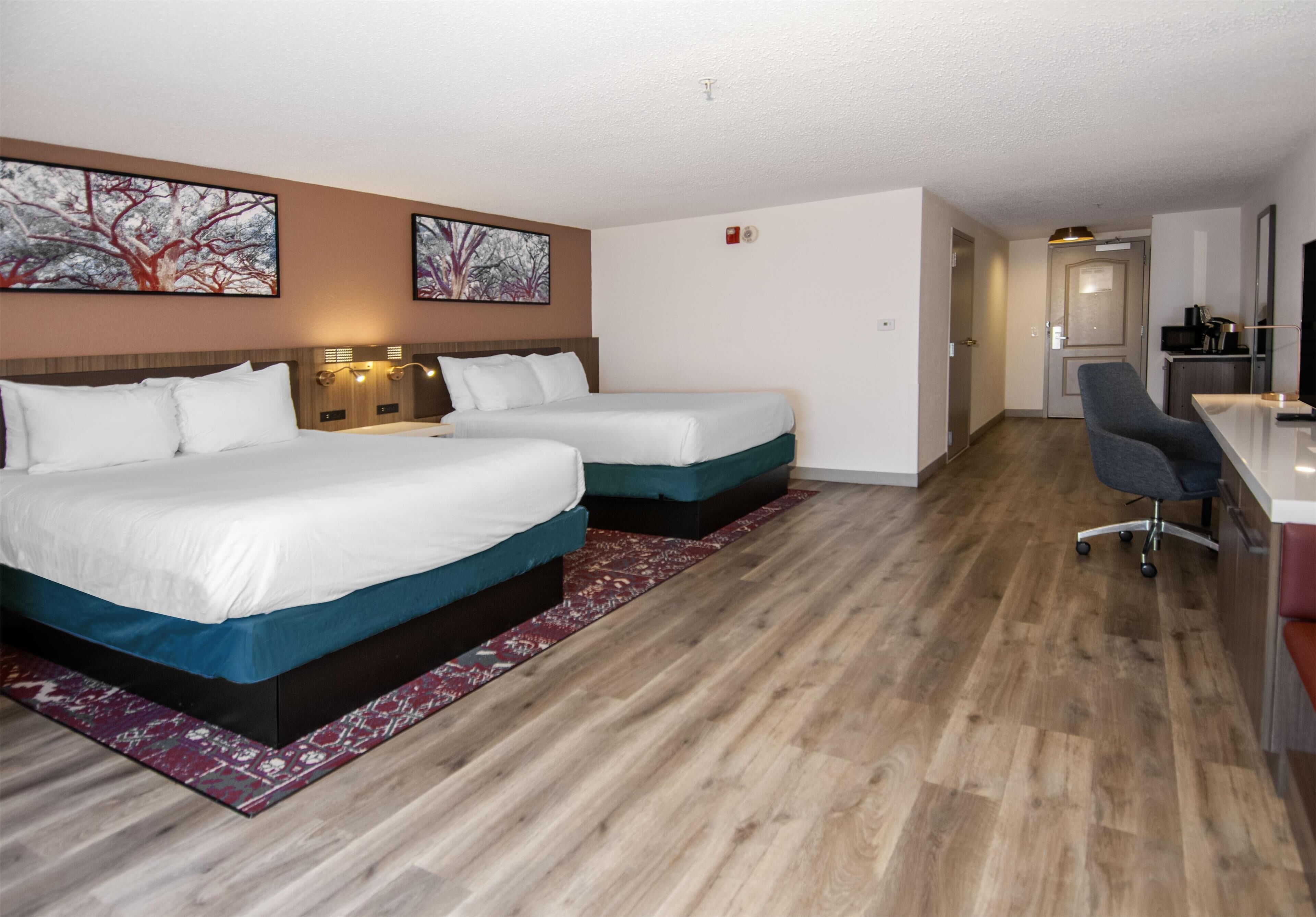 Quarto de hotel com duas camas, uma escrivaninha e uma cadeira.