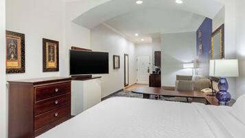 Quarto de hotel com cama, penteadeira, televisão de tela plana, escrivaninha, cadeira, abajur e porta que dá para outro cômodo.
