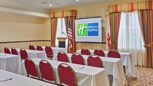 Uma sala de conferências com fileiras de mesas e cadeiras, um púlpito e uma tela de projeção exibindo o logotipo do Holiday Inn Express.