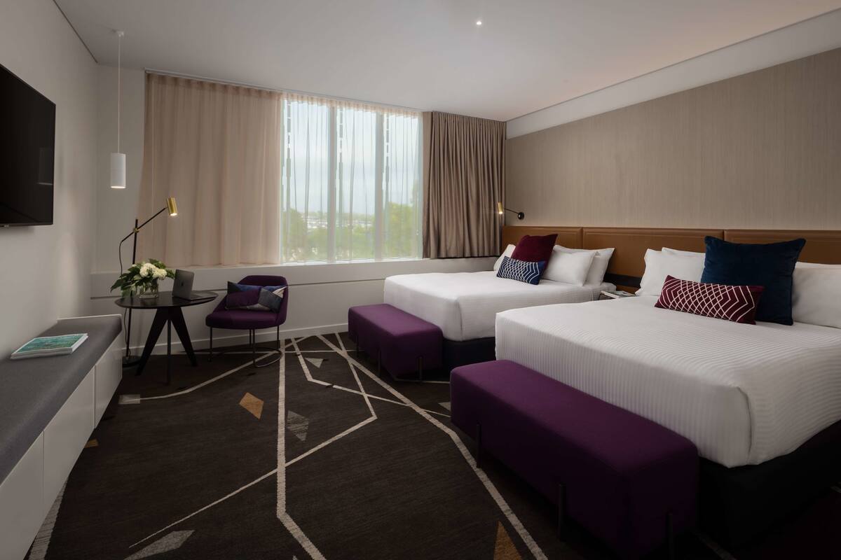 Quarto de hotel com duas camas, uma escrivaninha, uma cadeira e uma televisão.