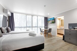 Quarto de hotel com duas camas, área de refeições, banheiro e um quadro na parede.
