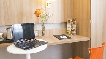 Um balcão de recepção de hotel com um laptop, um vaso de flores, uma cafeteira e um quadro de menu.