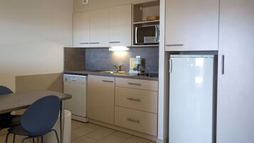 Uma cozinha compacta equipada com lava-louças, micro-ondas e frigorífico. Inclui uma mesa de jantar com cadeiras.