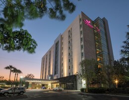Um hotel com vários andares, um letreiro chamativo, estacionamento e uma entrada bem iluminada.