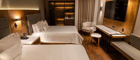 Quarto de hotel com duas camas, uma escrivaninha, uma cadeira, uma mesinha e uma televisão.