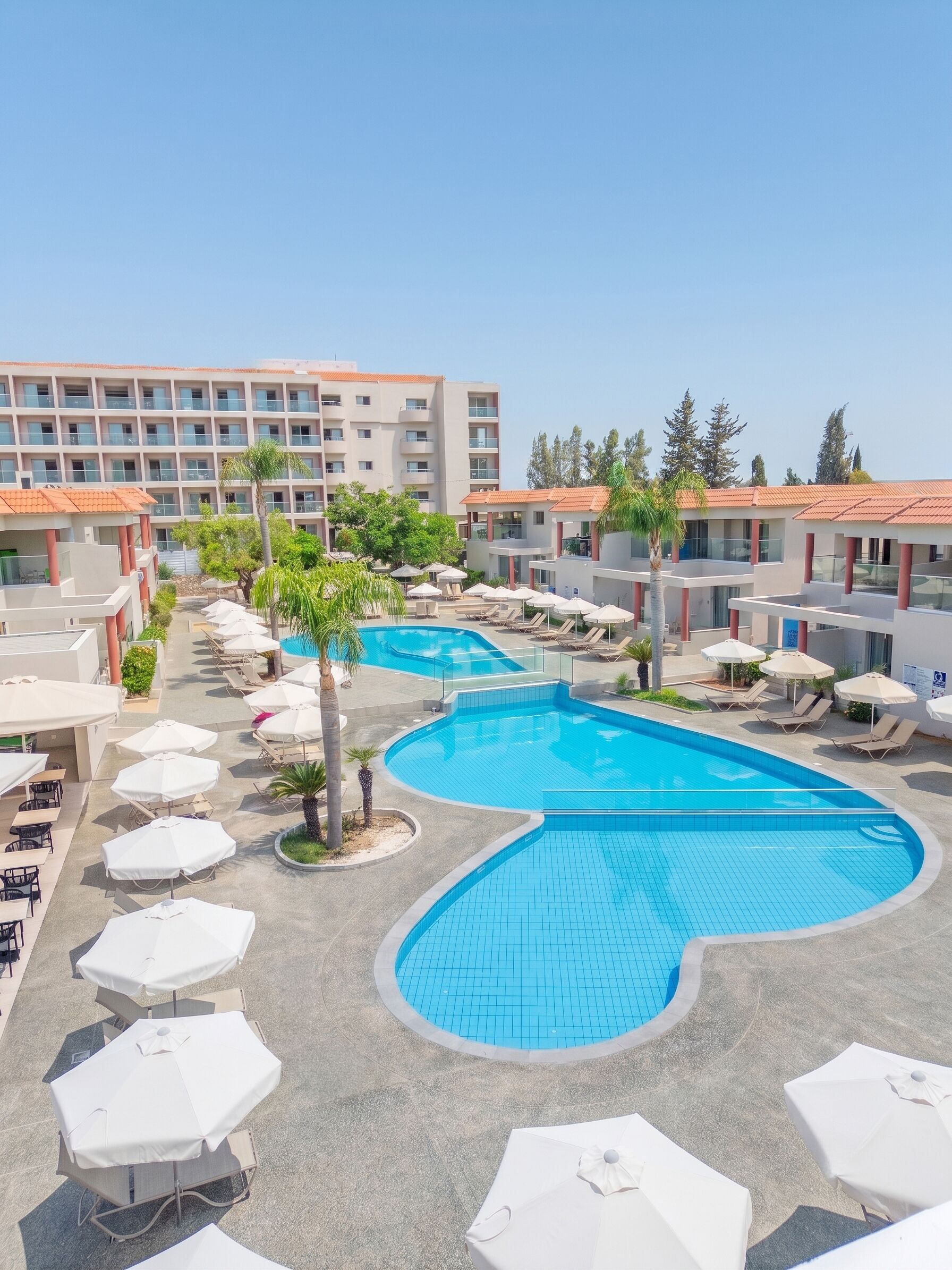 Uma área de piscina de hotel com várias piscinas, espreguiçadeiras e guarda-sóis.