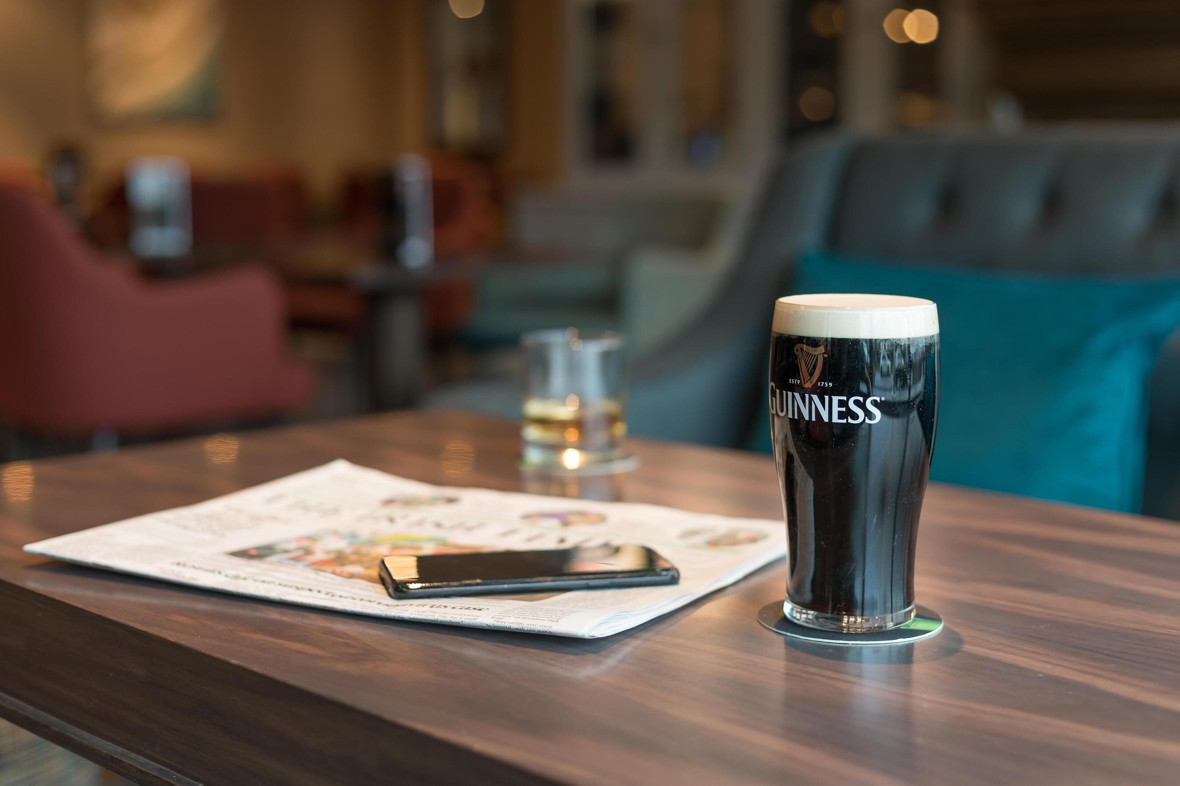 Uma mesa com um copo de cerveja Guinness, um jornal e um smartphone.