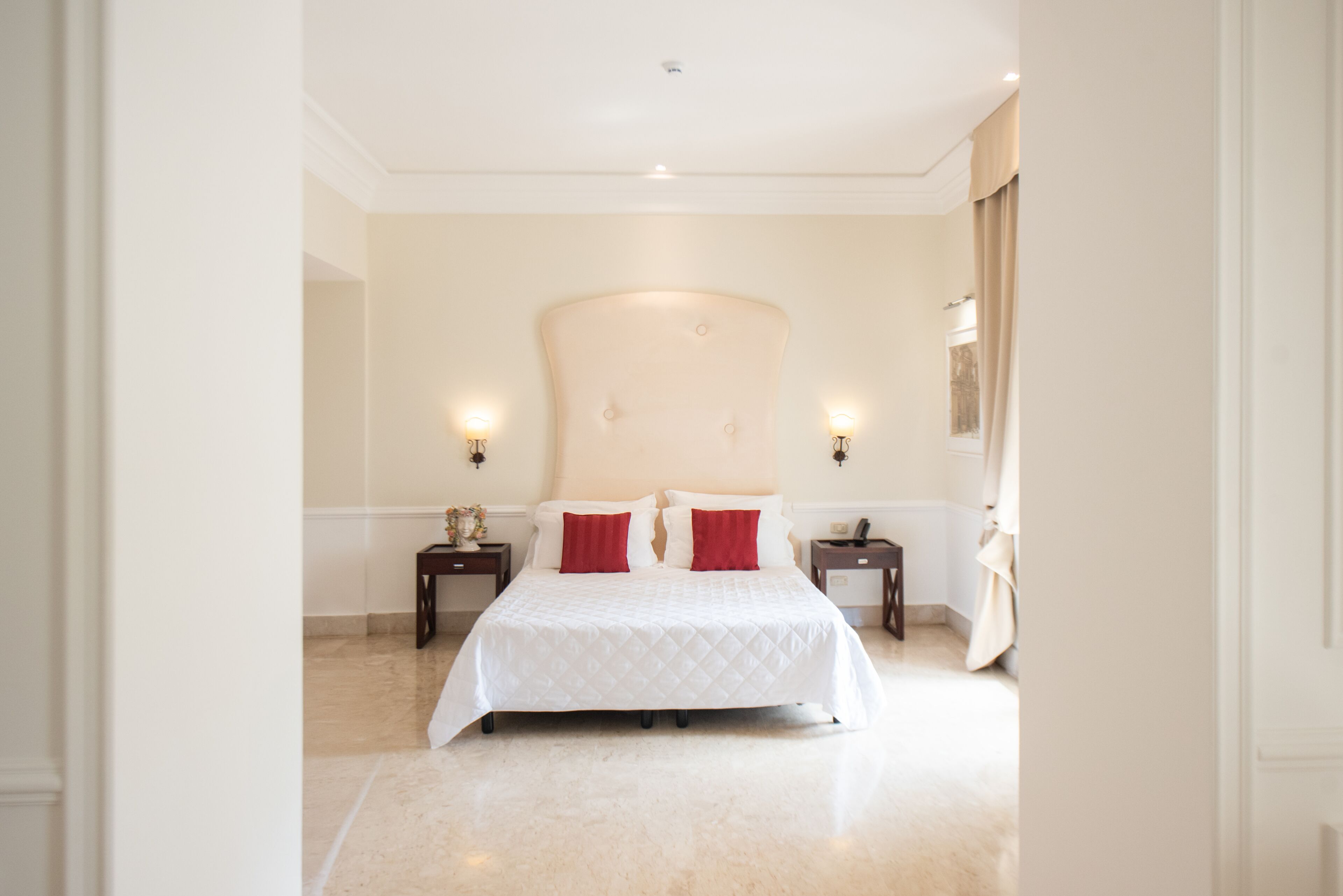 Quarto de hotel com uma cama grande, duas mesas de cabeceira, um painel de cabeceira e arandelas.