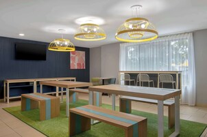 Quarto moderno com mesas e bancos de madeira, uma TV de tela plana e três luminárias pendentes.