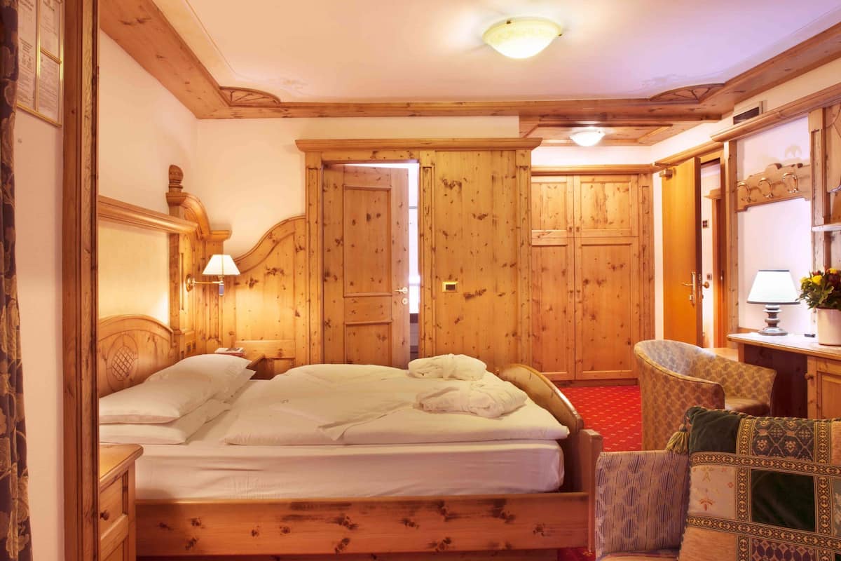 Um quarto de madeira com uma cama, uma cadeira e uma escrivaninha com abajur.