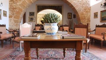 Um quarto com uma mesa de madeira, cadeiras, um tapete estampado e um vaso grande com uma planta.