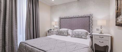 Quarto moderno com uma cama grande, mesas de cabeceira, um criado-mudo, um quadro na parede e um ar condicionado.