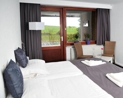 Quarto de hotel com cama, cadeira, janela com cortinas e vista para o exterior.