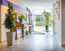 Um corredor com um piano, plantas em vasos e uma porta de vidro que dá para uma área externa.