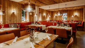 Restaurante com paredes de madeira e assentos vermelhos, com várias mesas e luminárias pendentes.