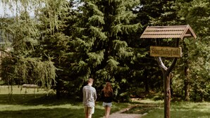 Um sinal de madeira com cobertura metálica em um parque com árvores e uma trilha.