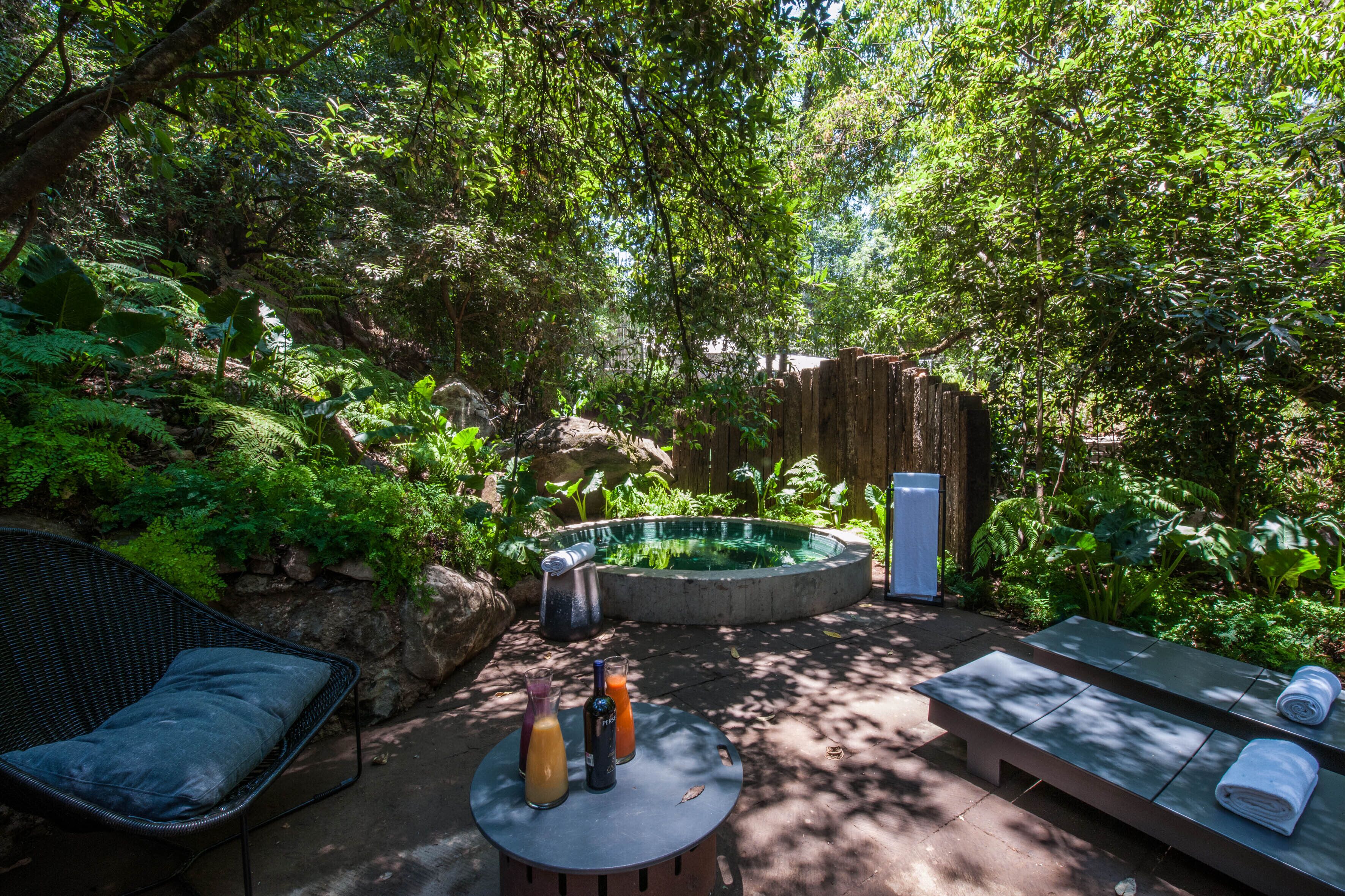 Um pátio exterior tranquilo com hidromassagem, cadeiras de descanso e uma mesa com bebidas.