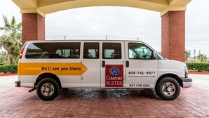 Uma carrinha branca com a marca 'Comfort Suites' e um número de telefone para reservas.
