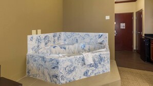 Um banheiro com banheira de mármore, um banco de madeira e uma porta ao fundo.