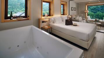 Quarto moderno com uma banheira grande, cama de casal, sofá e varanda com vista para a floresta.