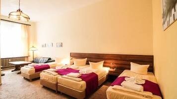 Quarto de hotel com três camas, uma cabeceira de madeira, uma mesa e um abajur.
