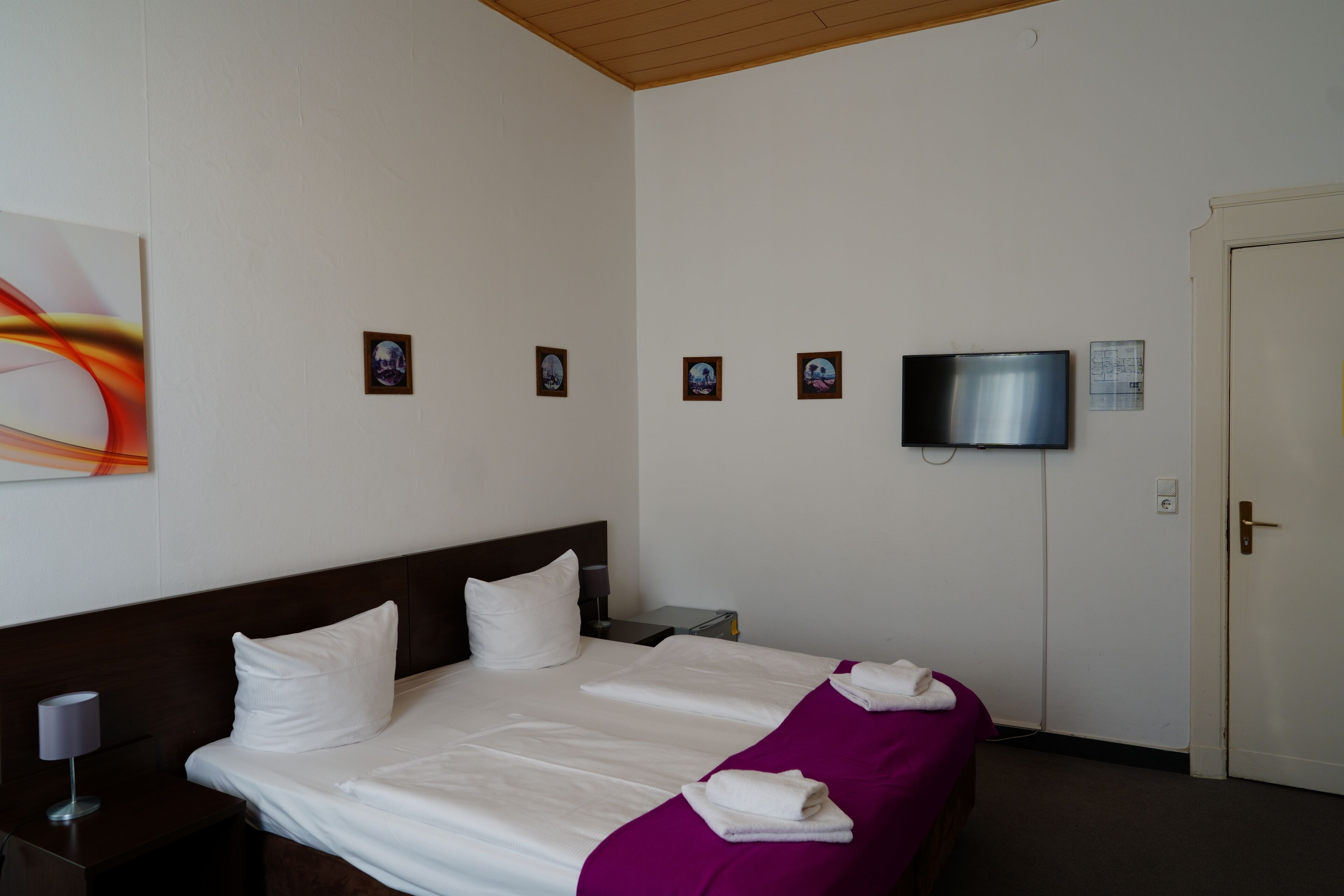 Quarto de hotel com uma cama, uma televisão fixada na parede e uma porta.