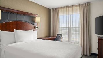 Quarto de hotel com uma cama grande, uma escrivaninha, uma cadeira, uma televisão e uma janela com cortinas.