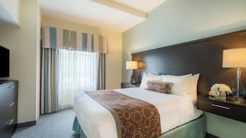 Quarto de hotel com uma cama grande, televisão, escrivaninha com abajur e janela com cortinas.