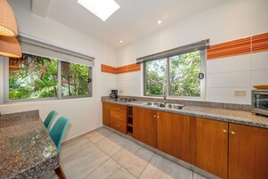 Cozinha moderna com armários de madeira, bancada de granito, forno embutido e janela com vista para vegetação.