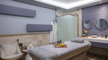 Uma sala de spa moderna com uma mesa de massagem, uma cadeira listrada, uma pequena mesa com garrafas e toalhas, e um lavatório com espelhos e artigos de higiene pessoal.