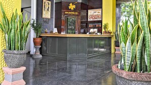 Uma área de recepção com balcão de madeira escura, obras de arte emolduradas e plantas em vasos.