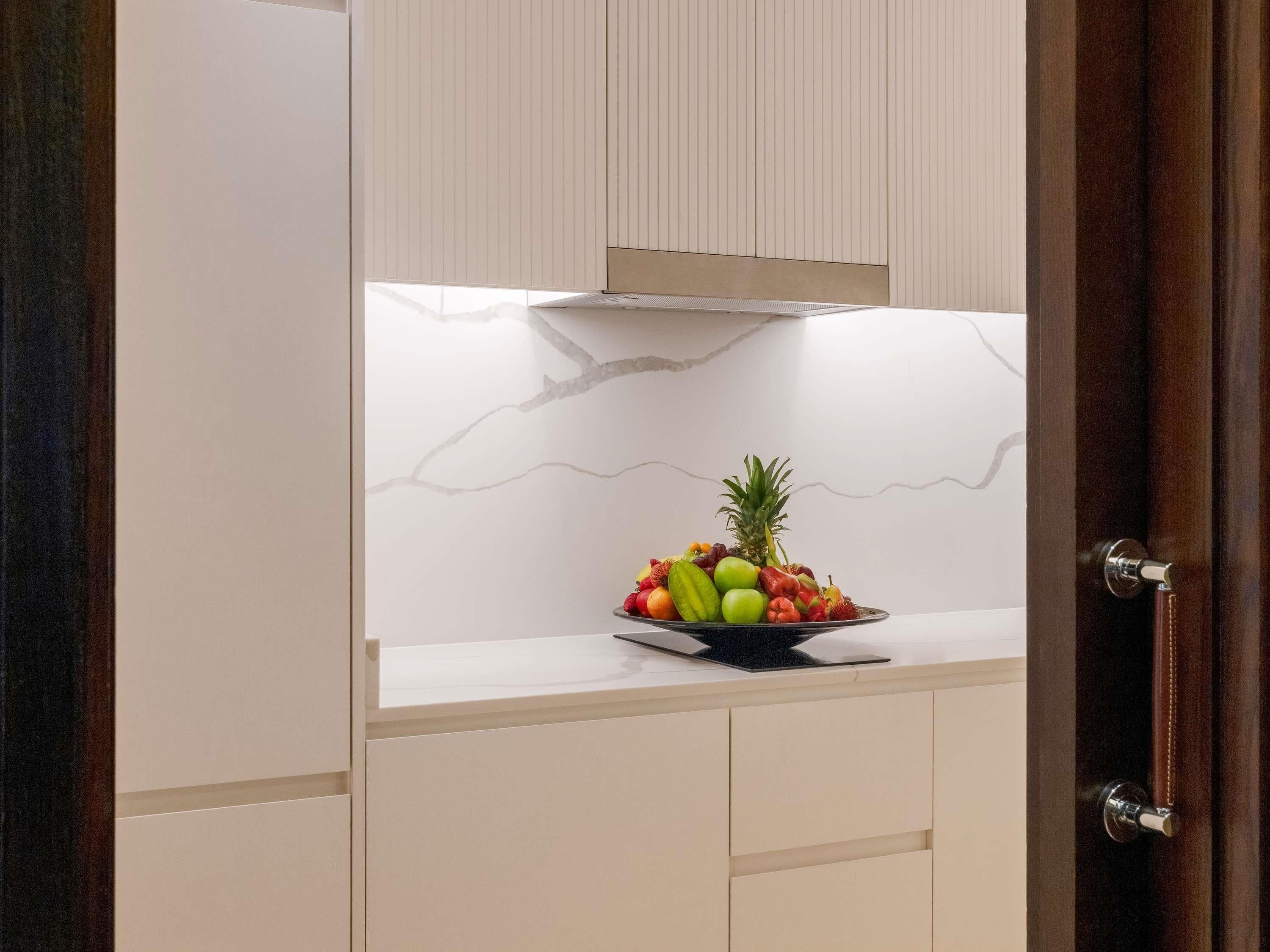 Uma cozinha com revestimento de mármore, uma fruteira no balcão e uma porta de madeira.