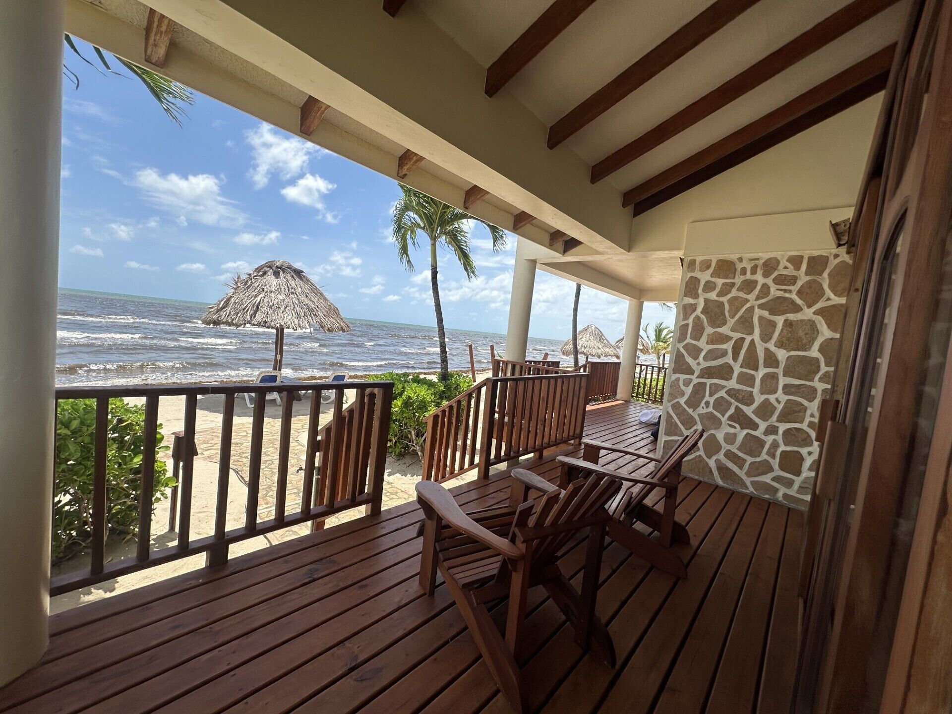 Um deck de madeira com cadeiras e uma mesa, com vista para o oceano e guarda-sóis de palha.