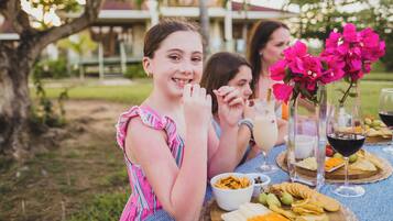 Um grupo de pessoas sentadas numa mesa ao ar livre, com comida e bebida.