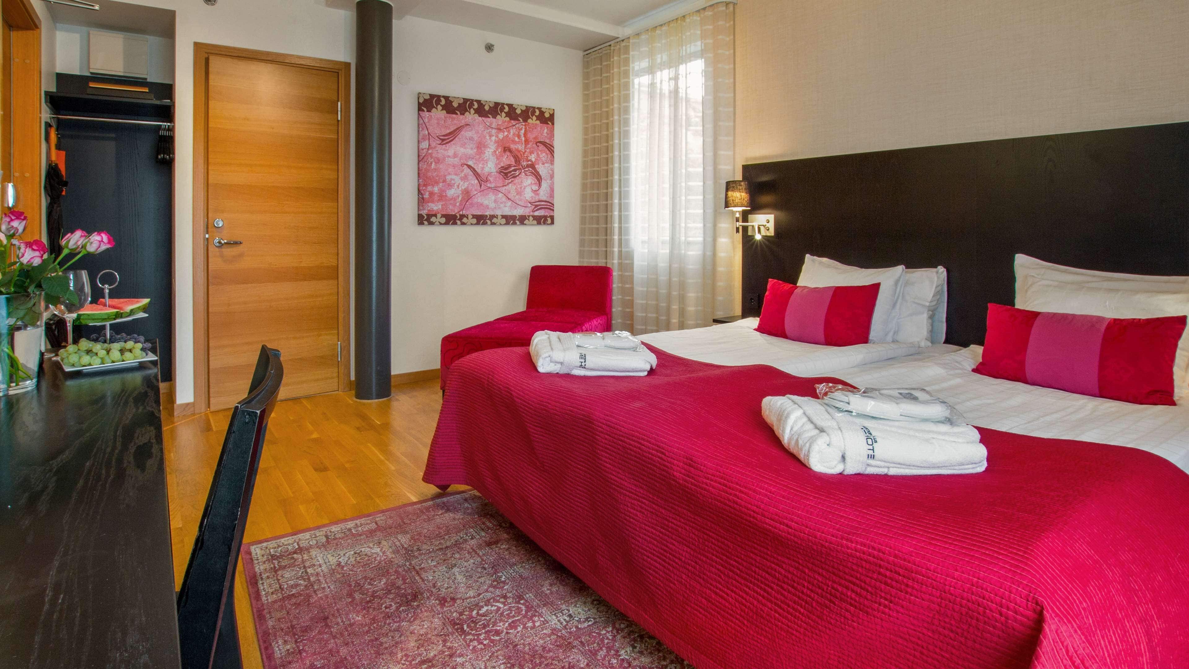 Quarto de hotel com uma cama grande, uma cadeira vermelha, uma porta de madeira e um quadro na parede.