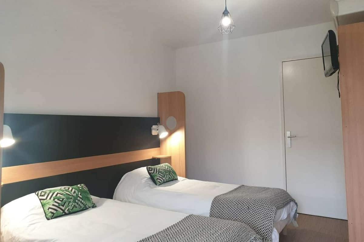 Quarto de hotel com duas camas, cabeceira de madeira, televisão fixada na parede e uma porta.