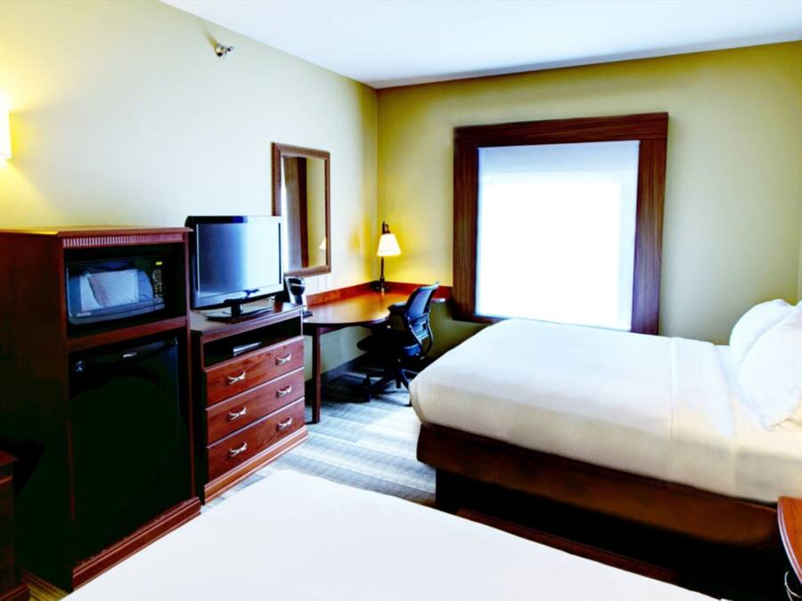 Quarto de hotel com cama, escrivaninha, computador, televisão e telefone.