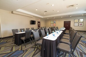 Uma sala de conferência com uma mesa comprida, cadeiras, garrafas de água e quadros nas paredes.