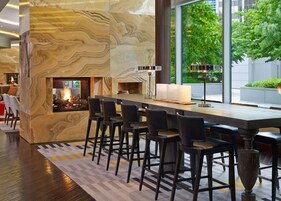 Uma área de bar moderna com parede de mármore, banquetas e uma janela ampla que oferece vista para o verde lá fora.