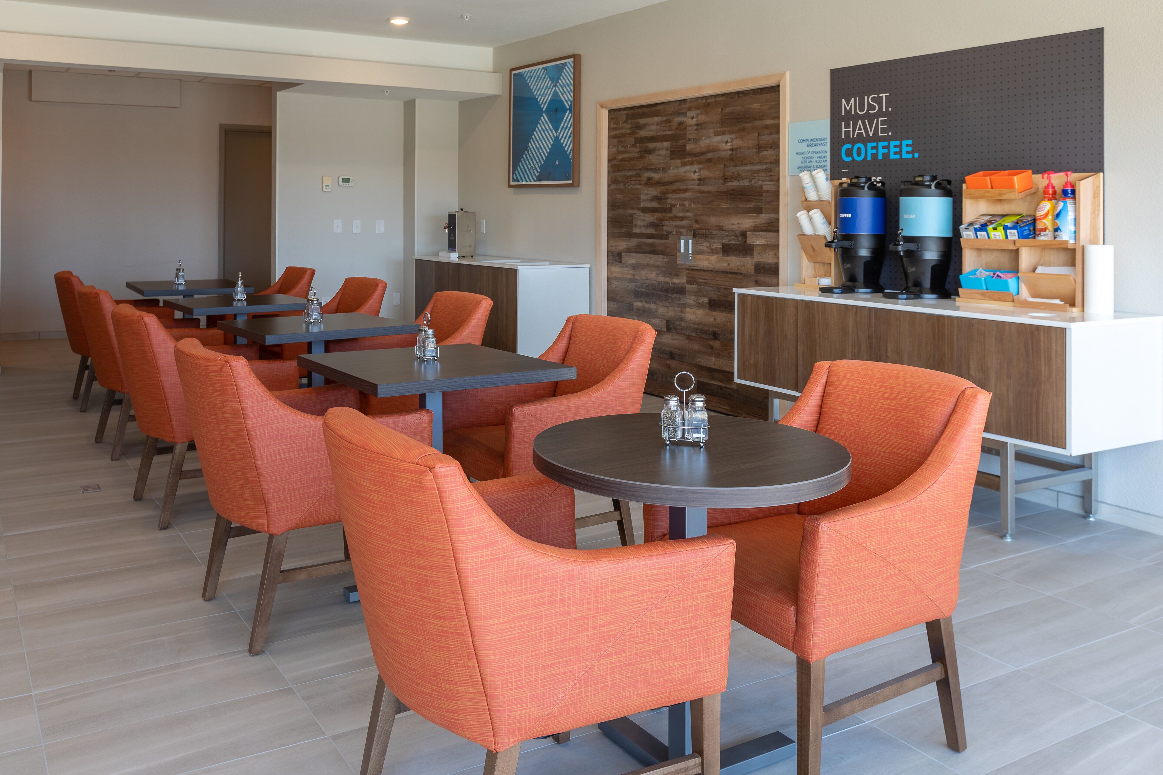 Um lobby de hotel moderno com diversas áreas de estar, um espaço com café e uma parede com uma frase motivacional.