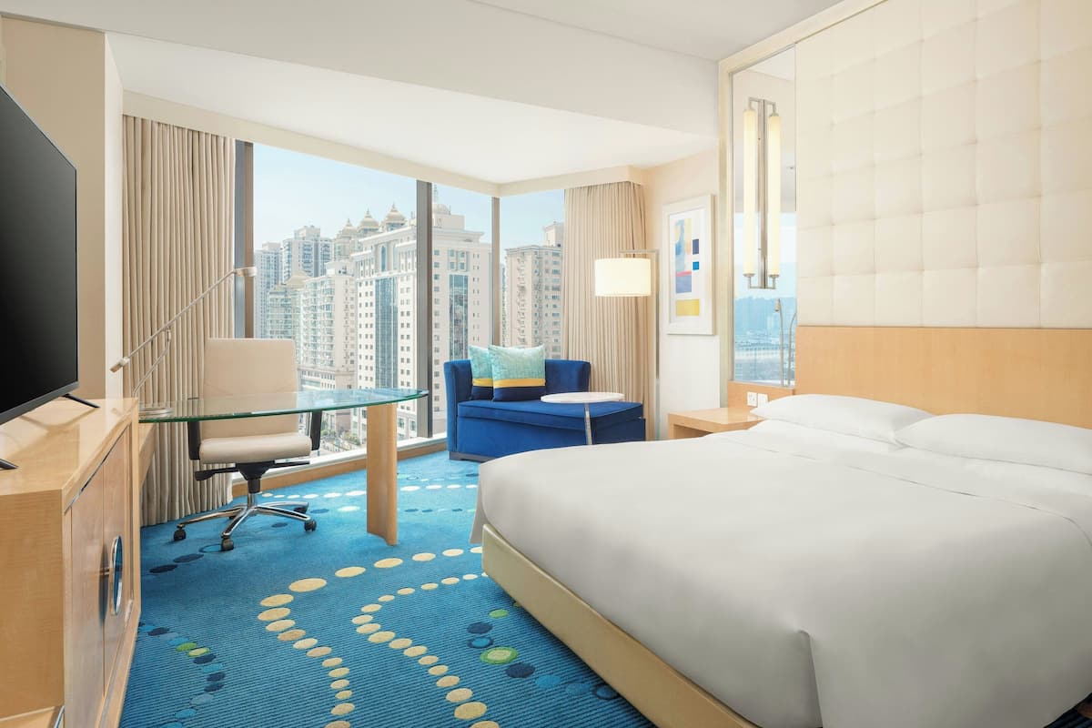 Quarto de hotel com uma cama grande, uma escrivaninha com cadeira, um sofá e uma televisão.