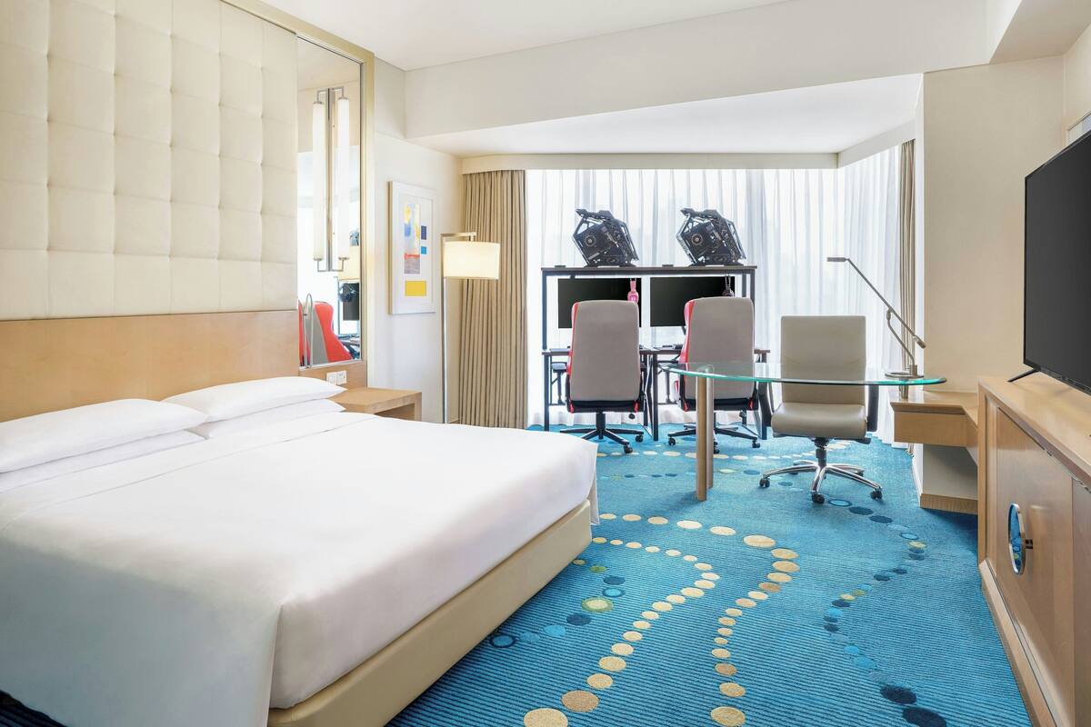 Quarto de hotel com uma cama grande, uma escrivaninha com computador e uma televisão.