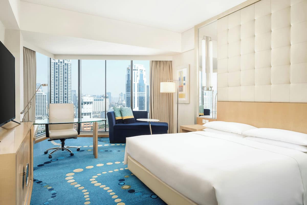 Quarto de hotel com cama grande, escrivaninha, cadeira e vista para a cidade.