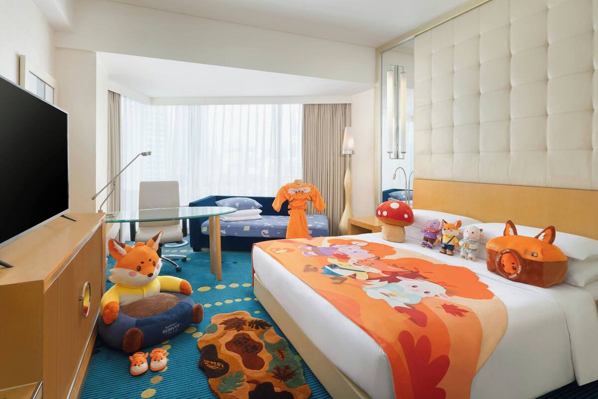 Quarto de hotel com uma cama grande, uma escrivaninha, televisão e brinquedos macios.