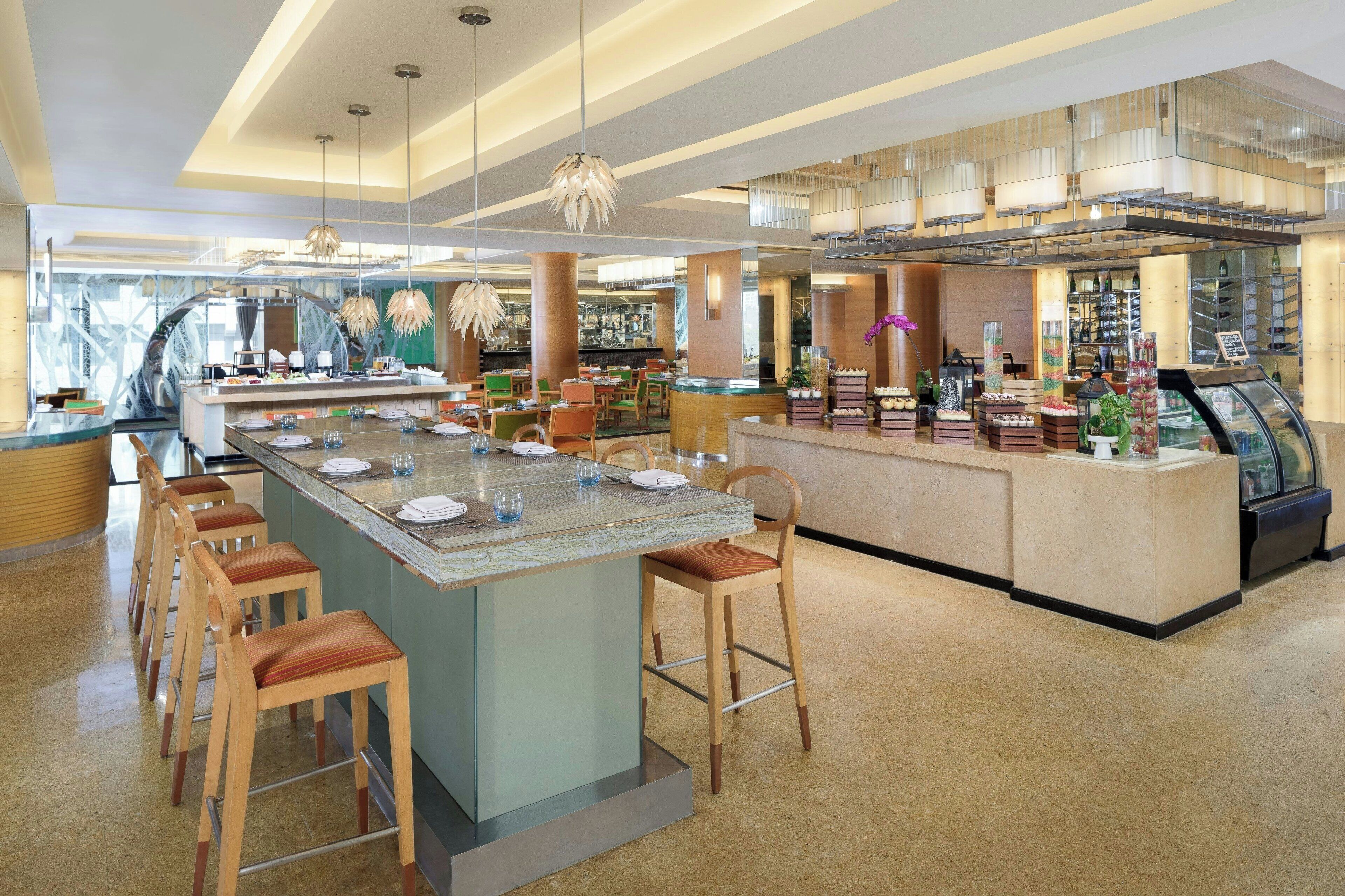 Um lobby moderno de hotel com área de bar central, disposições de assento e escadaria para um andar superior.