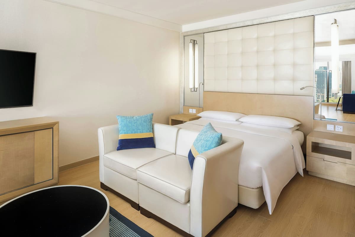 Quarto de hotel com cama, sofá, televisão e um espelho grande.