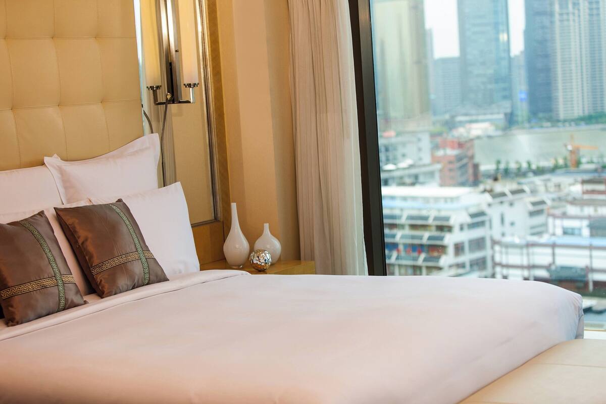Quarto de hotel com uma cama grande, vista para o horizonte urbano e uma janela com cortinas.